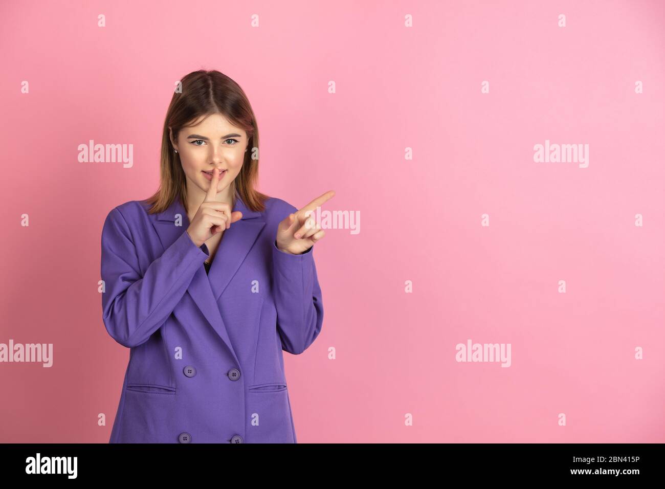 Pointing secretly. Caucasian young woman's portrait isolated on pink ...