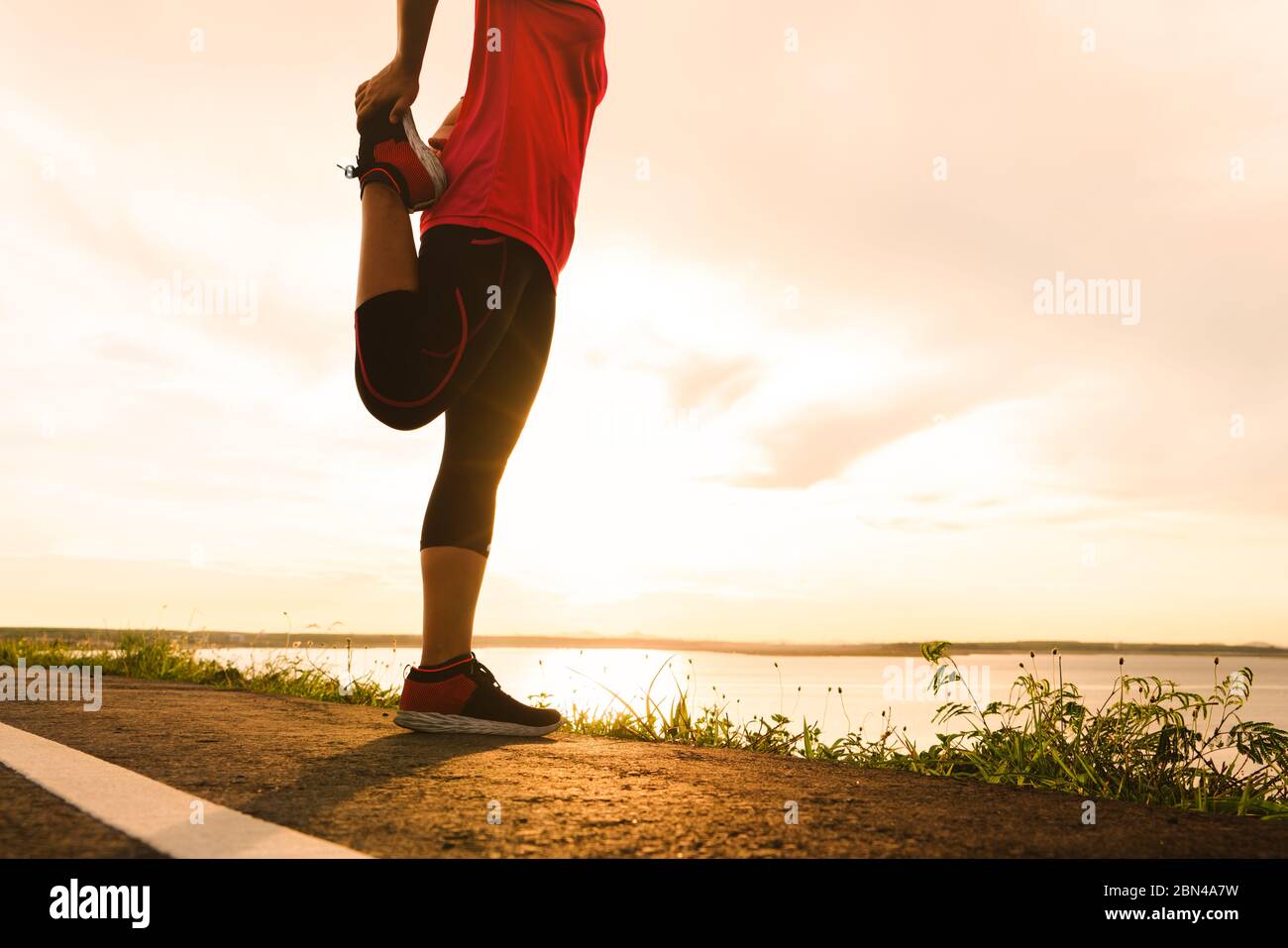 woman stretching leg muscle preparing for sunset trail run Stock Photo ...