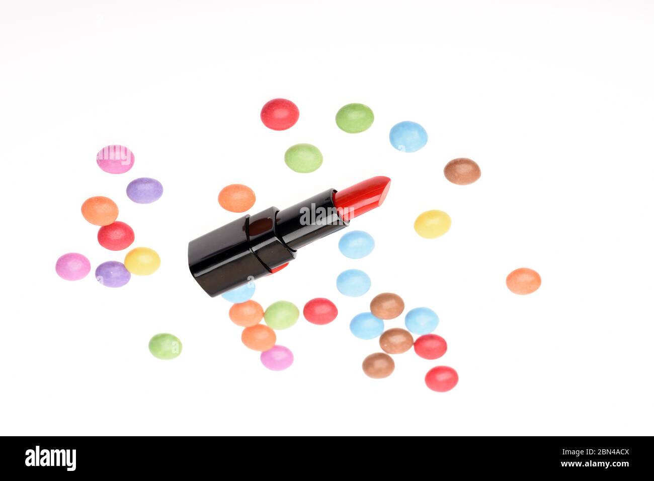 Red or scarlet lipstick on white background near colorful dragee sweets ...
