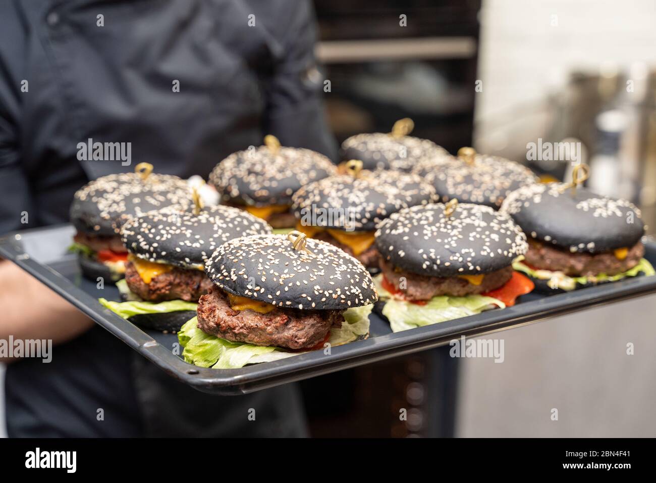 Chef showing a tray full of classic burgers with black buns Stock Photo ...