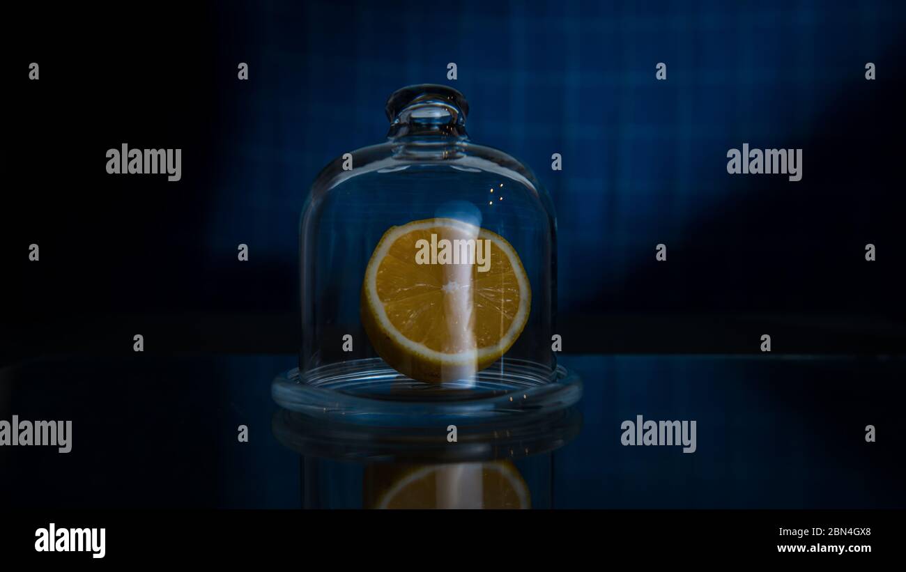 Half lemon in a glass lemon storage container on a dark blue background ...