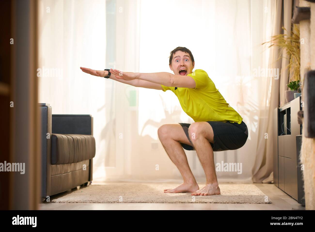 Man In T Shirt And Shorts Is Doing Squat Exercises At Home In His