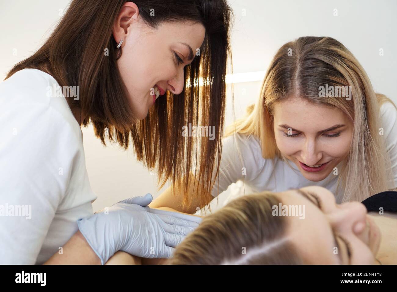 Two cheerful confident cosmetologists doing hair removal. Two happy ...