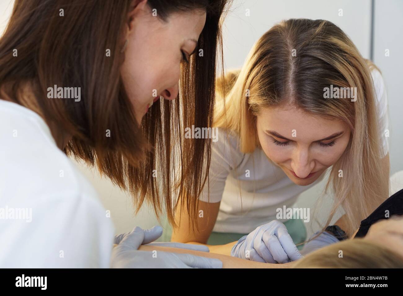 Two cheerful confident cosmetologists doing hair removal. Two happy ...
