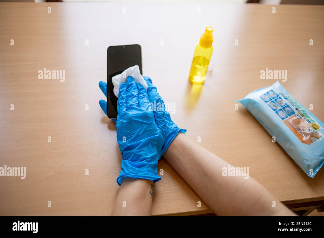 Woman's hand in blue gloves sanitizing cleaning smartphone mobile phone ...