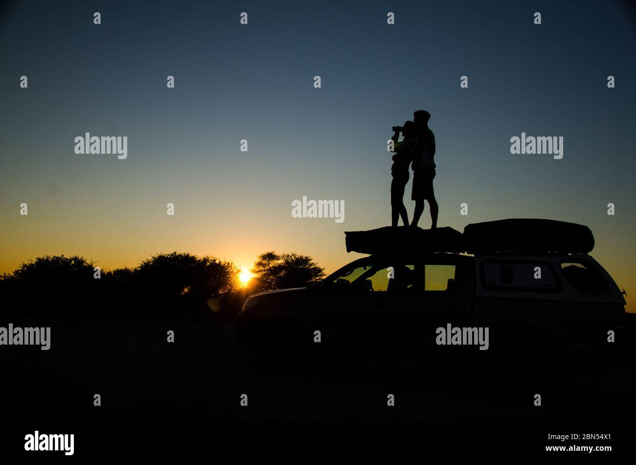 A couple standing on a jeep during sunset Stock Photo - Alamy