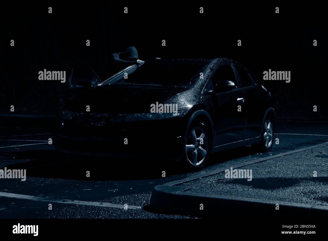A mysterious hooded figure, standing next to a car with the door open ...