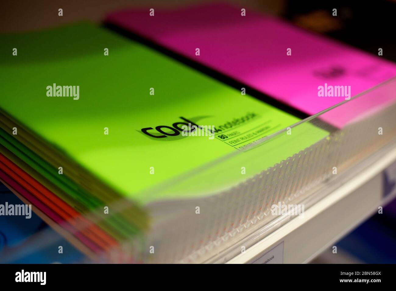 Bright green and pink coloured A4 exercise books stacked on a shelf ...