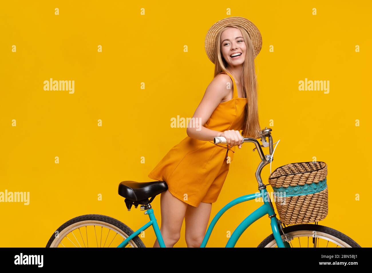 Beautiful young girl in summer clothes riding bike over yellow ...