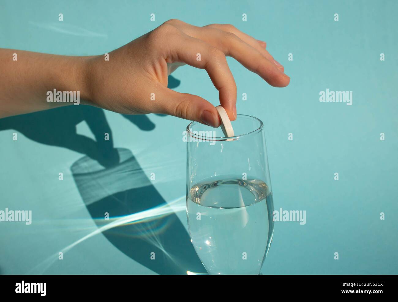 Against a blue background, a hand drops a dissolving fizzy aspirin ...