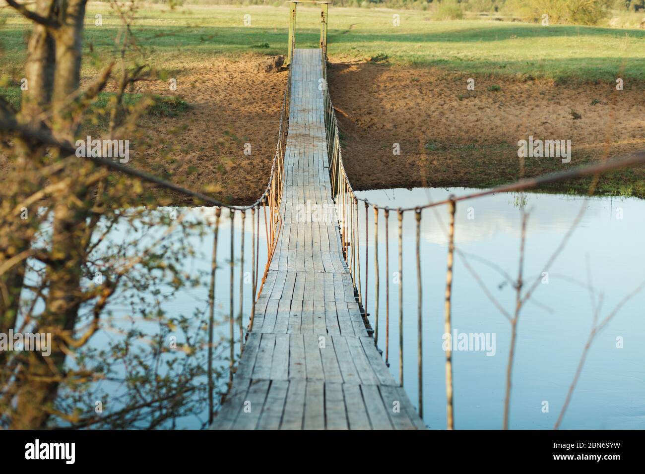 Old suspended wooden foot bridge over the river. Photo on a summer day ...