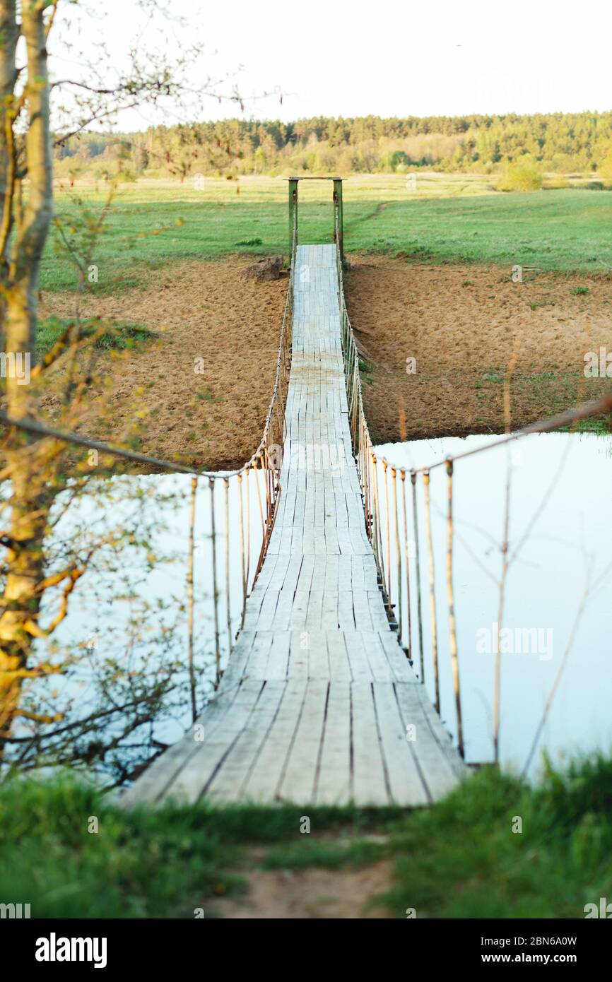 Old suspended wooden foot bridge over the river. Vertical photo on a ...