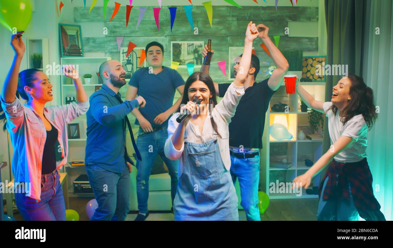 Beautiful young woman singing a song on microphone while partying with ...