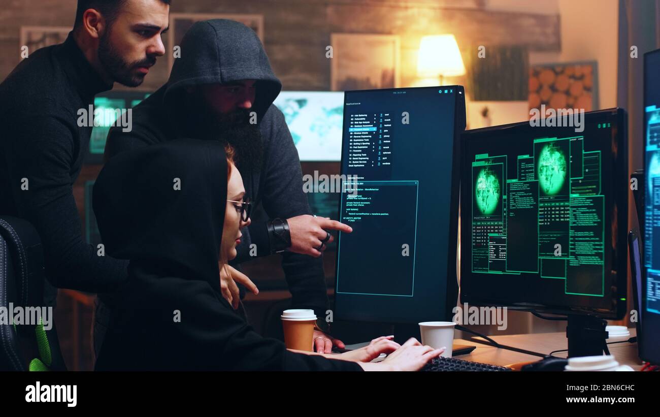 Team of hackers looking at computer with multiple monitors while ...