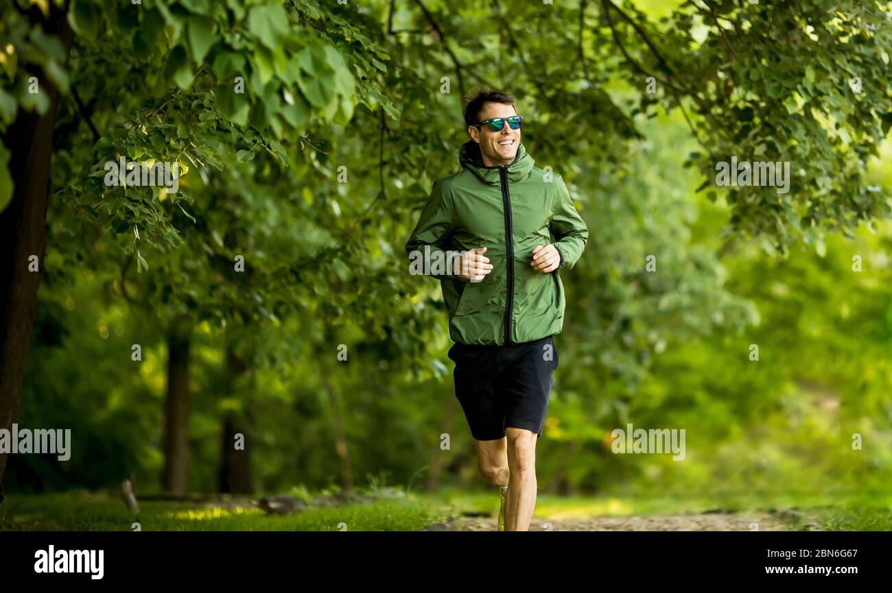 Athletic handsome young man running while doing workout in sunny green ...