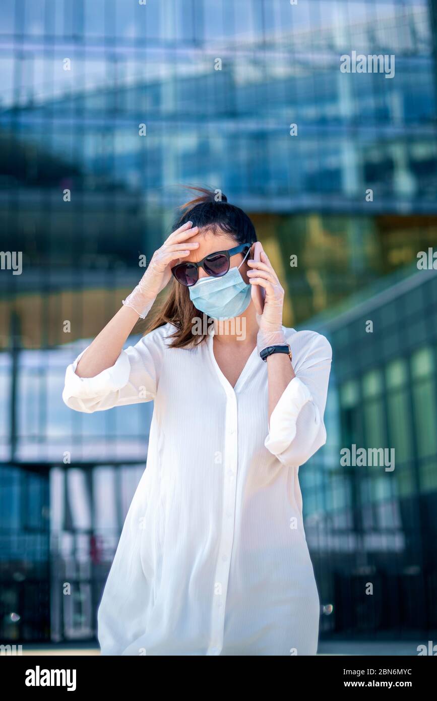Careworn woman wearing face mask and touching her head while standing ...