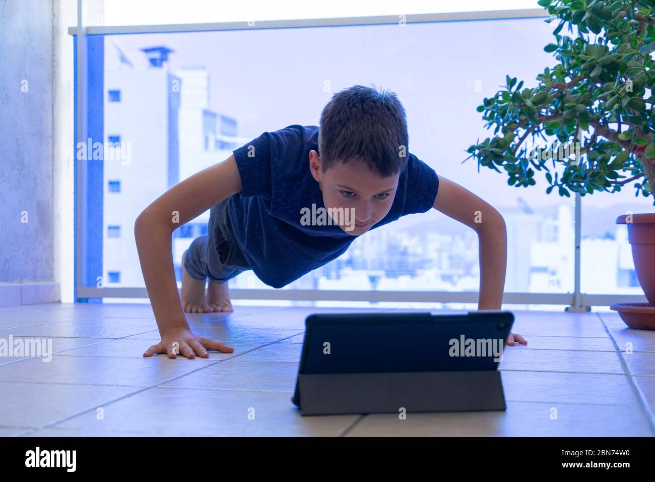 Kid with tablet computer doing push-ups sport exercises on balcony ...