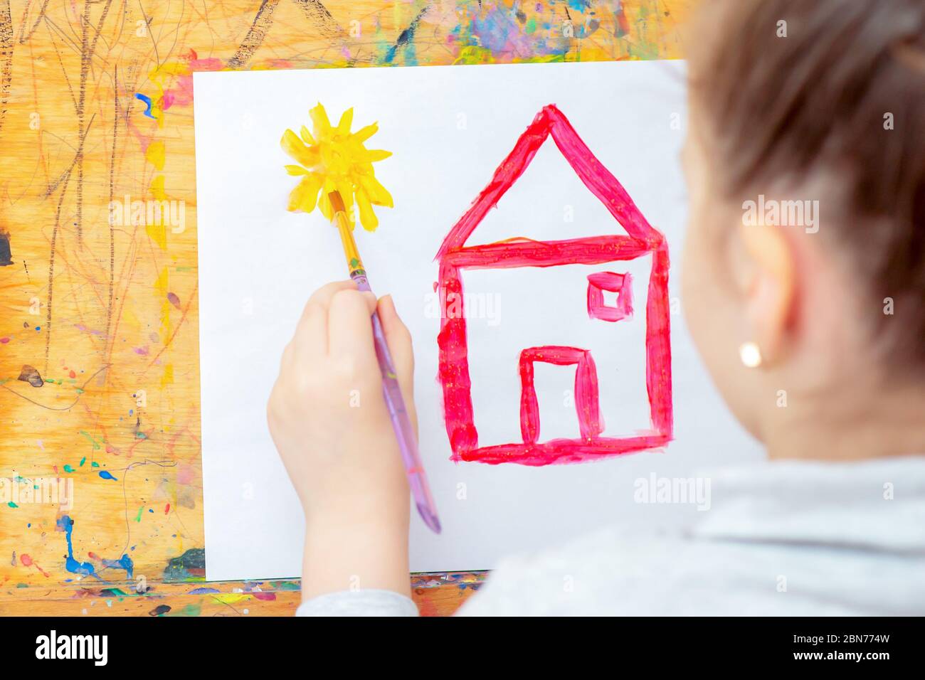 Little girl is drawing yellow sun and red house with watercolors on ...