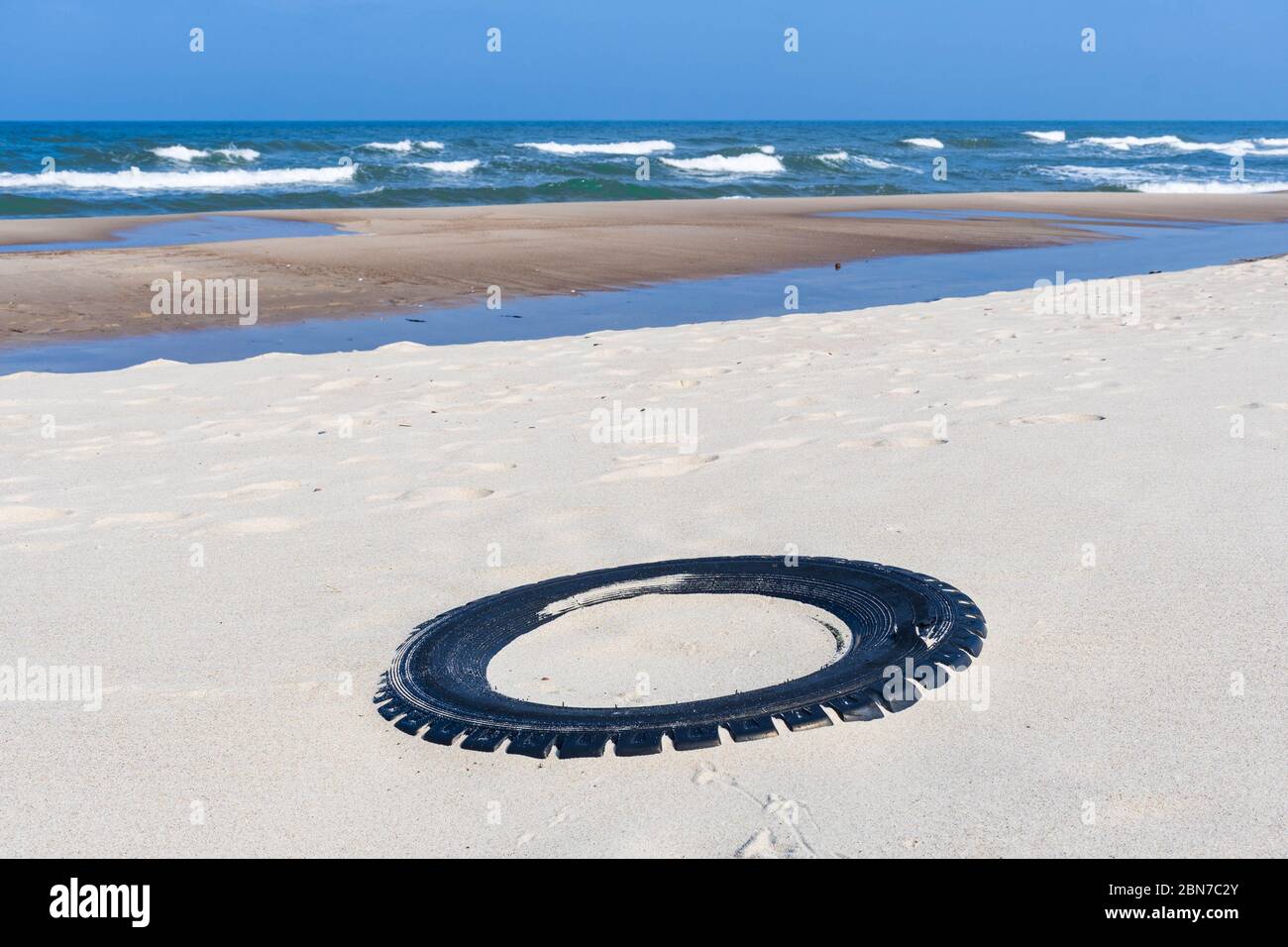 Big black rubber tire left on a sandy beach with blue sea and waves on ...