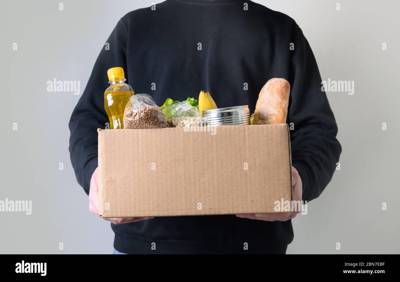 Volunteer holding donation food with goods. Box with oil, vegetables ...