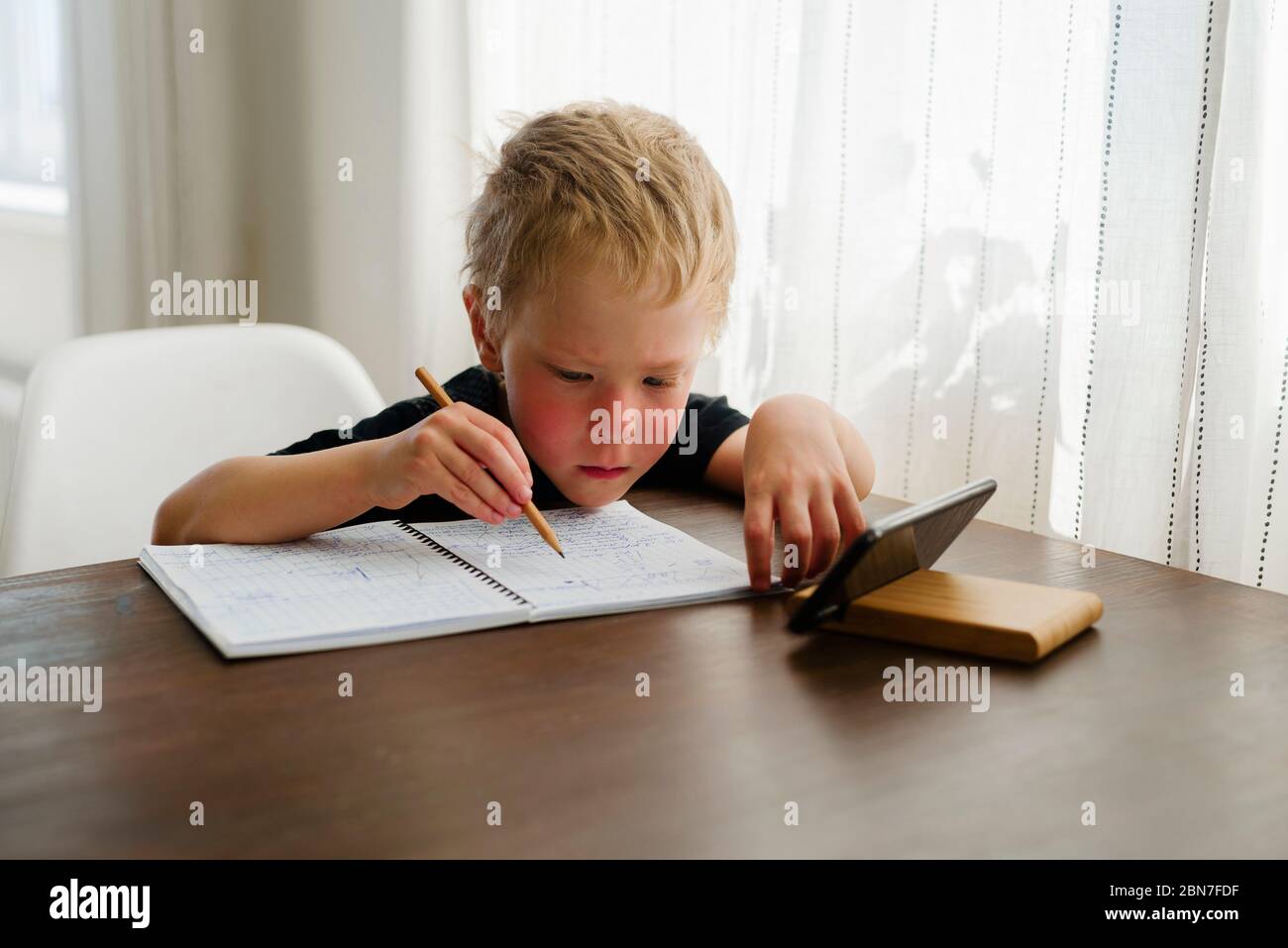 Little sad and tired boy learning at home. Watching webinar by mobile ...