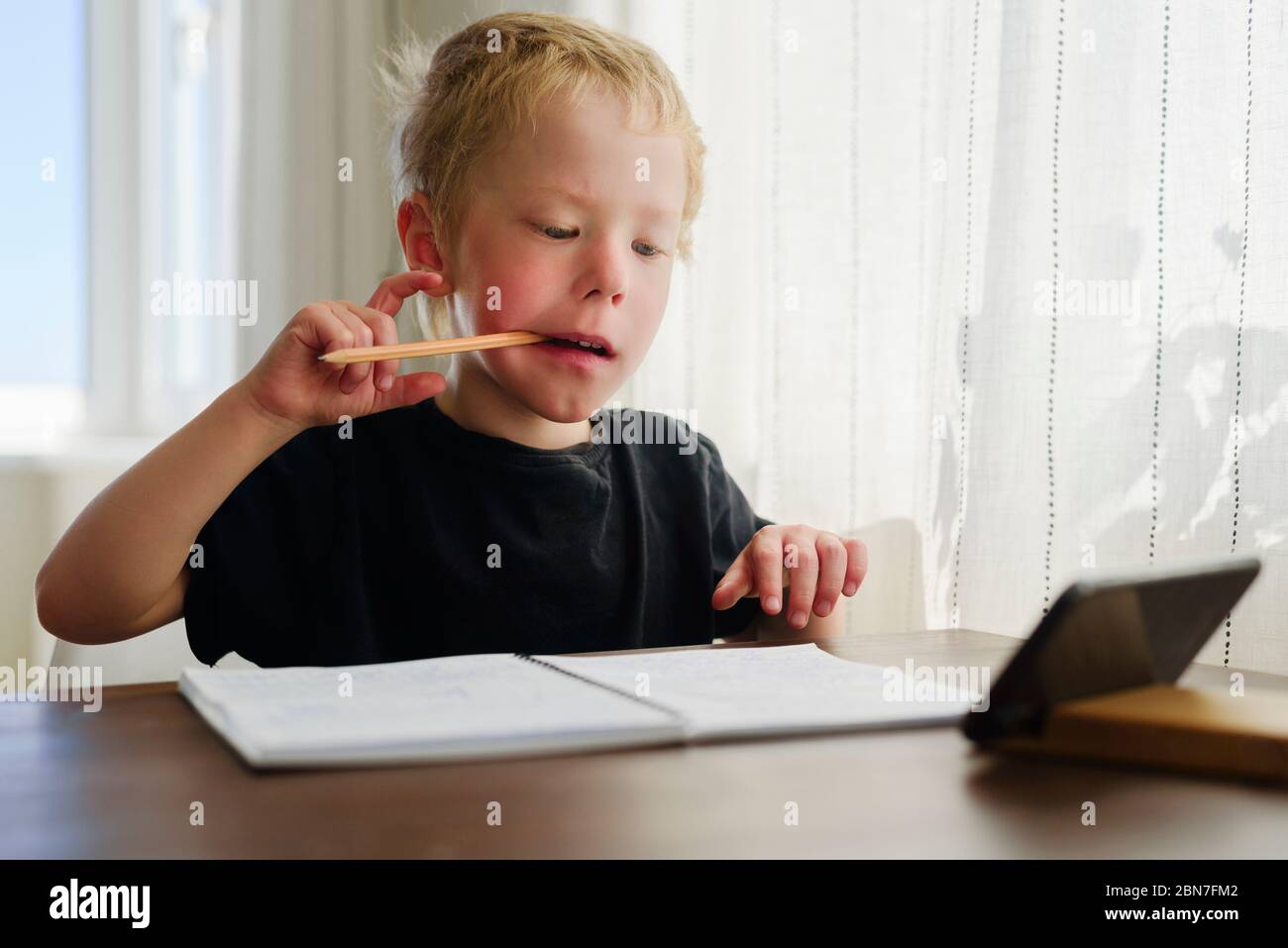 Little boy learning at home. Watching webinar by mobile, writing in ...