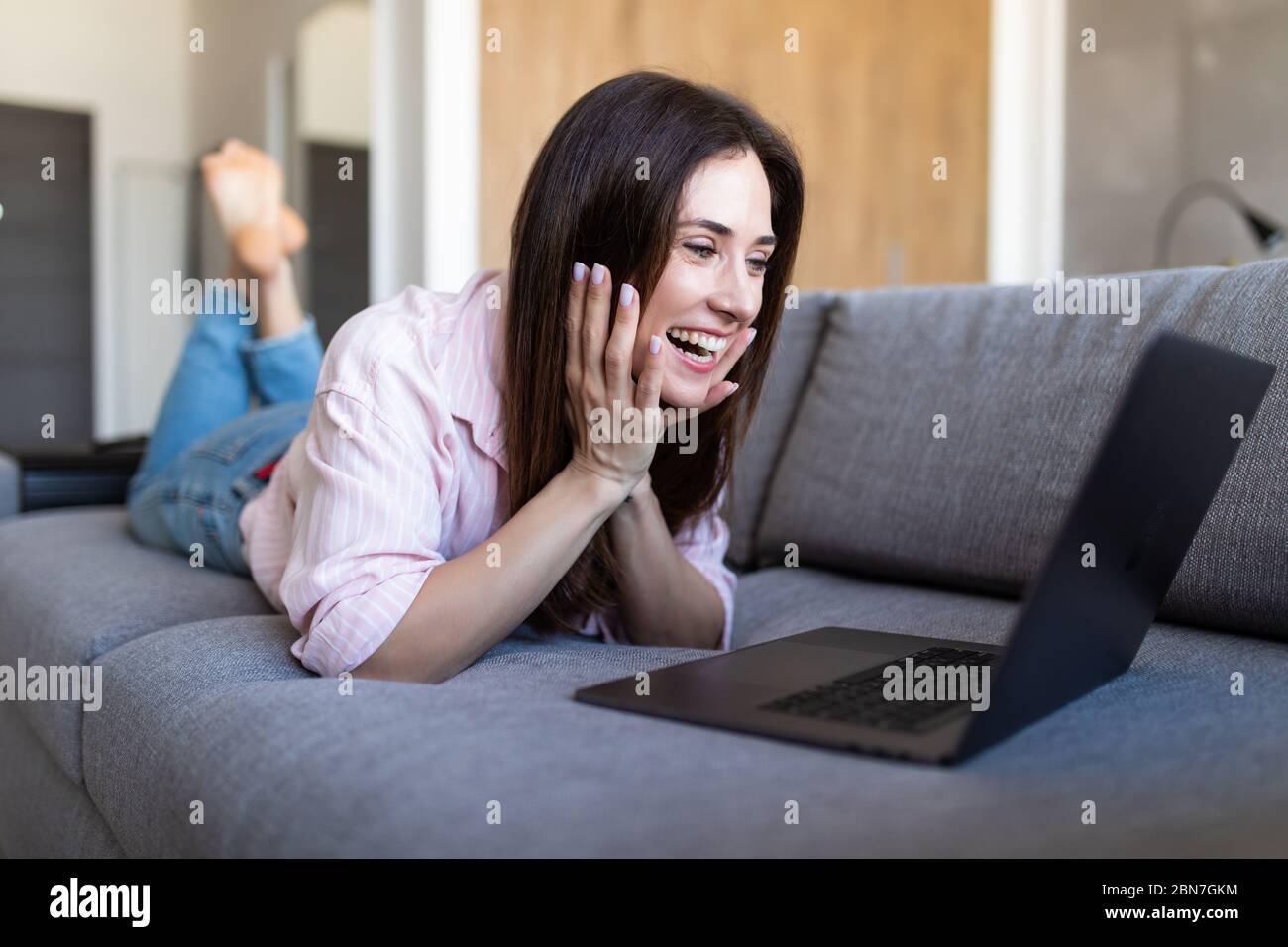 Happy girl lying on couch using laptop at home in the living room Stock ...