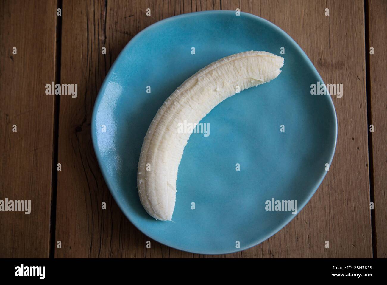 peeled banana inside a blue plate on top of a wooden table ready to eat ...
