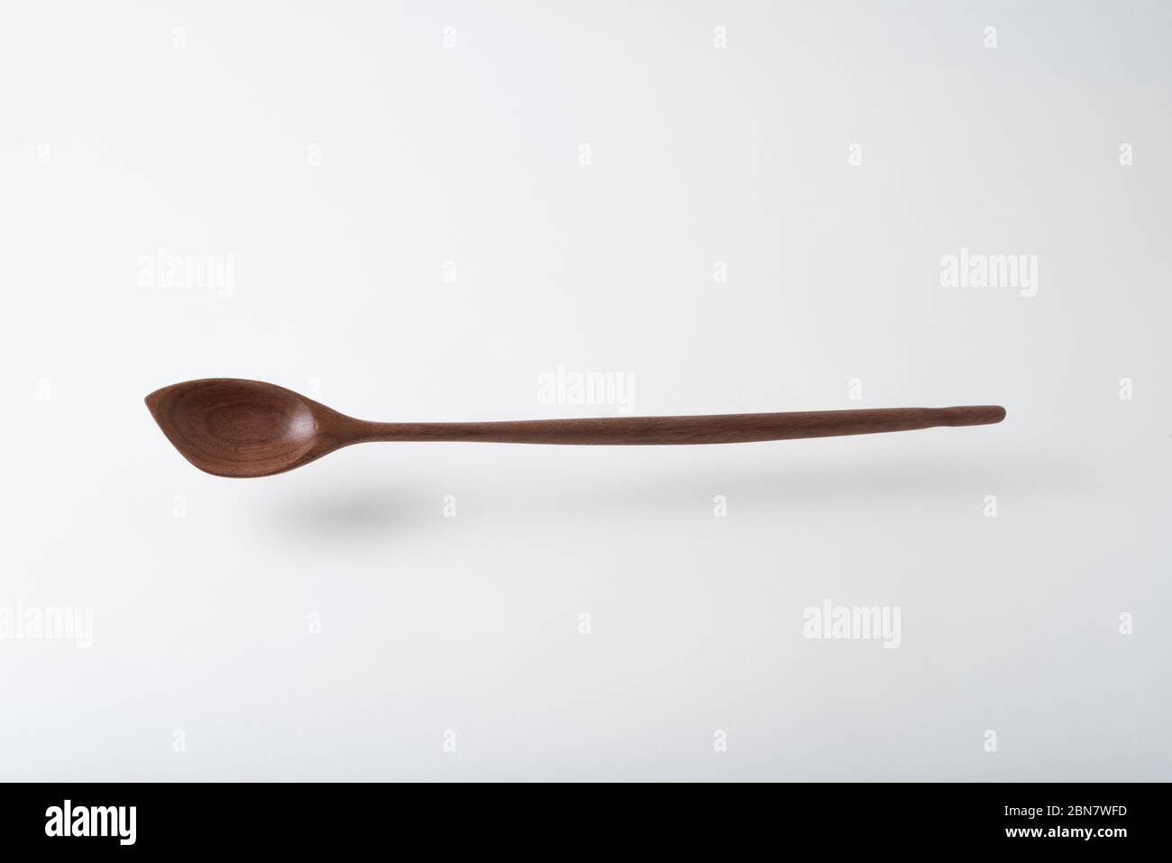 A long, handmade spoon from walnut wood, photographed against a plain ...