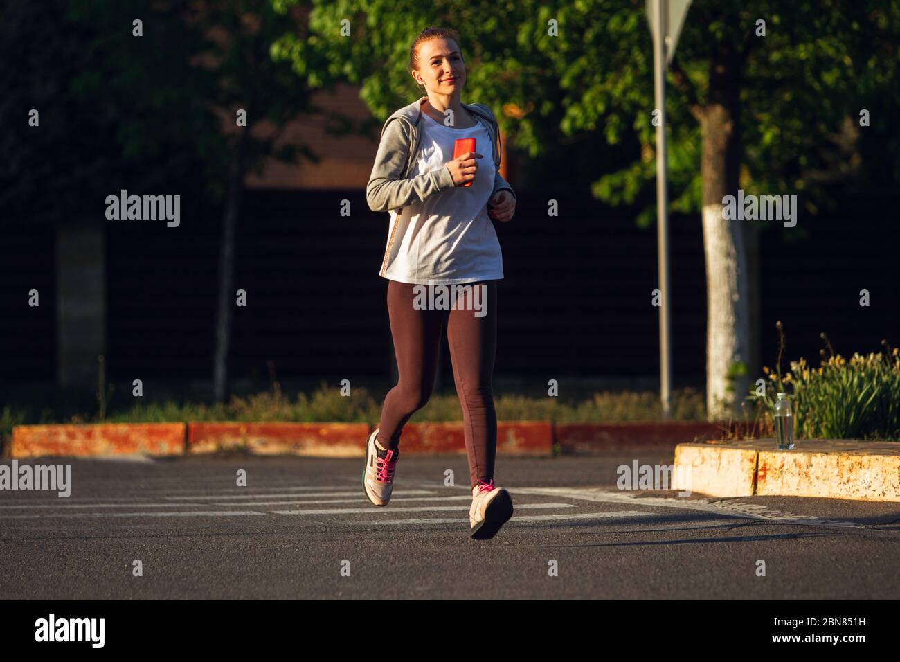 Young female runner, athlete is jogging in the city street in spring sunshine. Beautiful ...