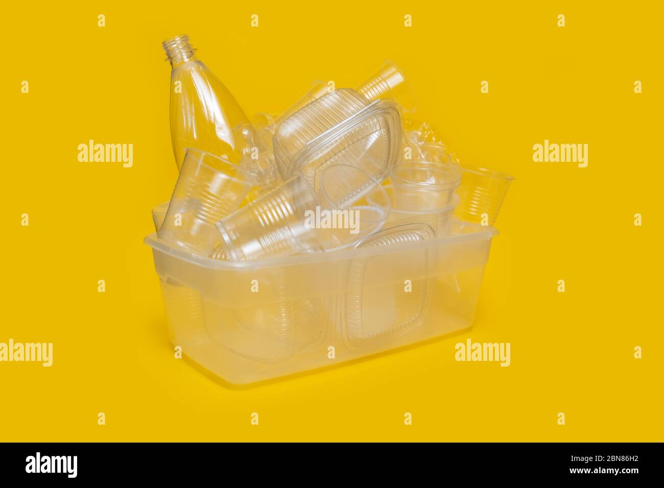 A lot of different plastic crockery and containers on yellow background ...