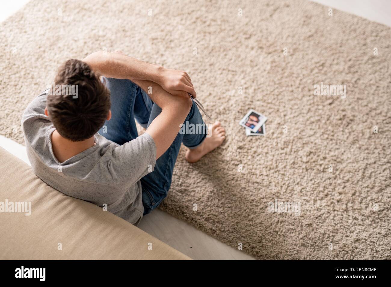 Above view of despondent man sitting on floor and thinking about old ...