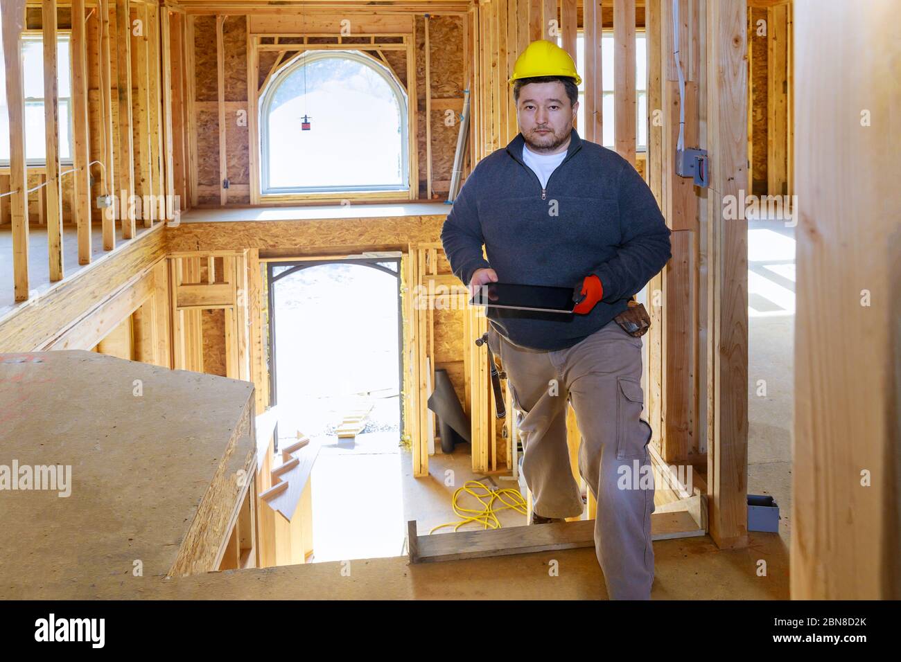 Building inspector looking at new home on holding tablet with hard hat ...