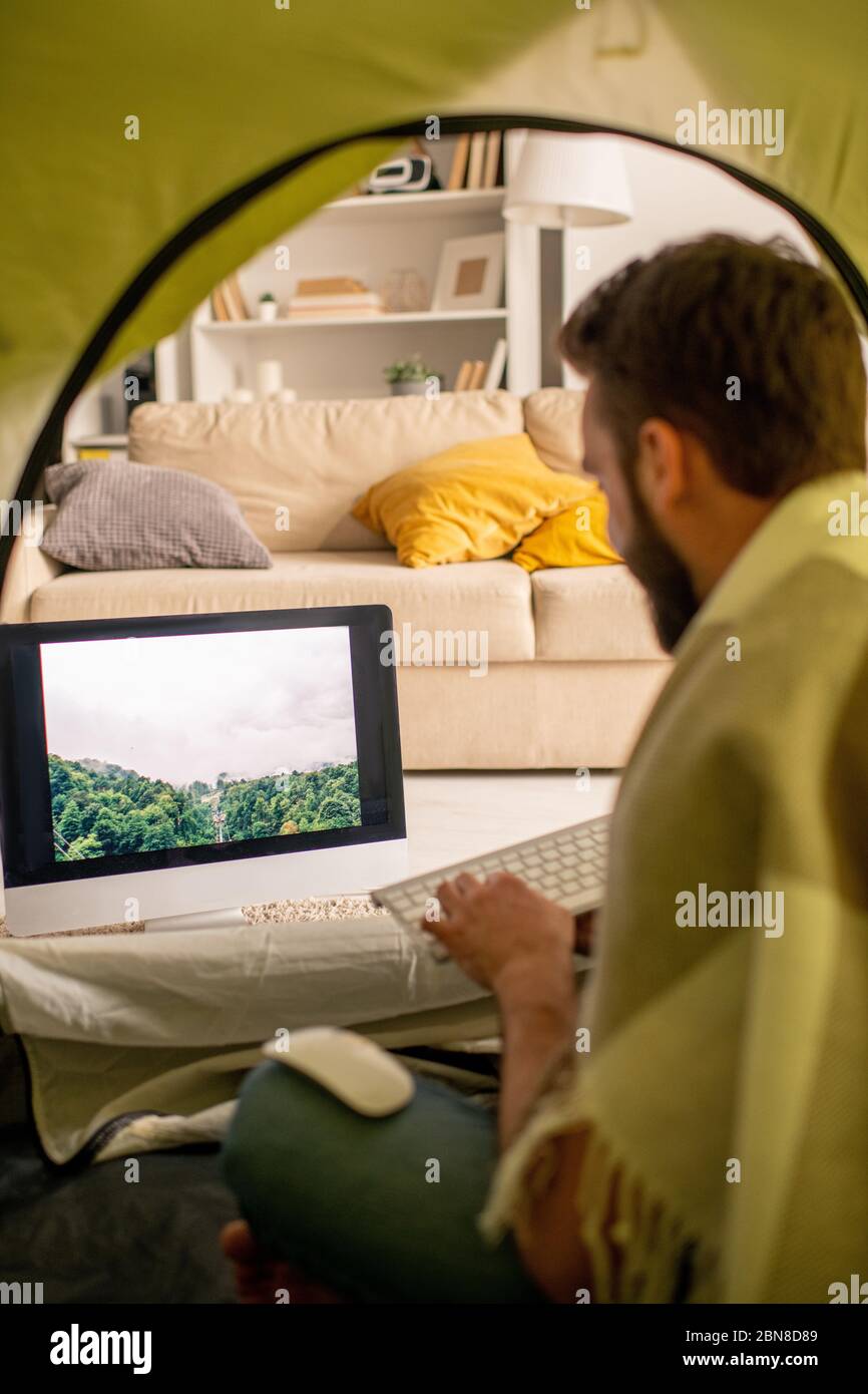 Over shoulder view of man under blanket sitting in tent at home and ...
