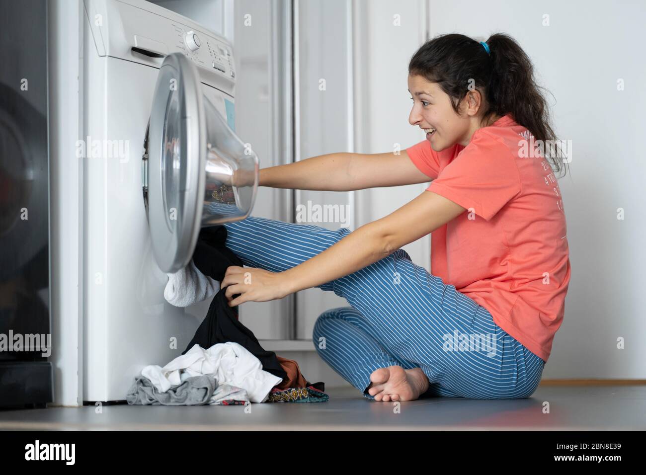 Girl kicks dirty laundry in the washing machine. A lot of dirty clothes ...