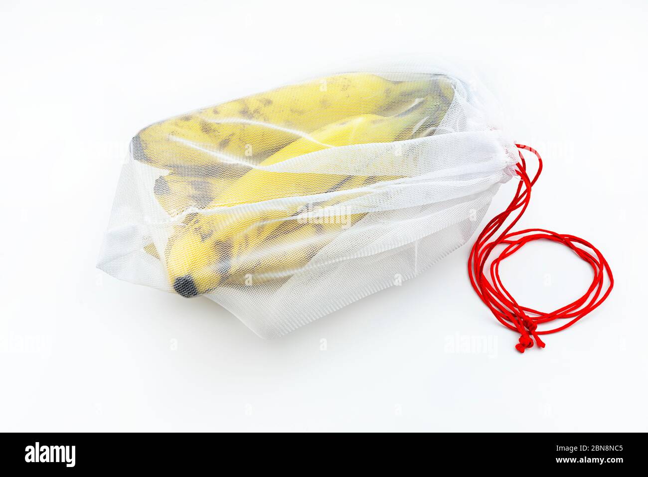 Ripe bananas packed in a white reusable mesh bag with red string ...