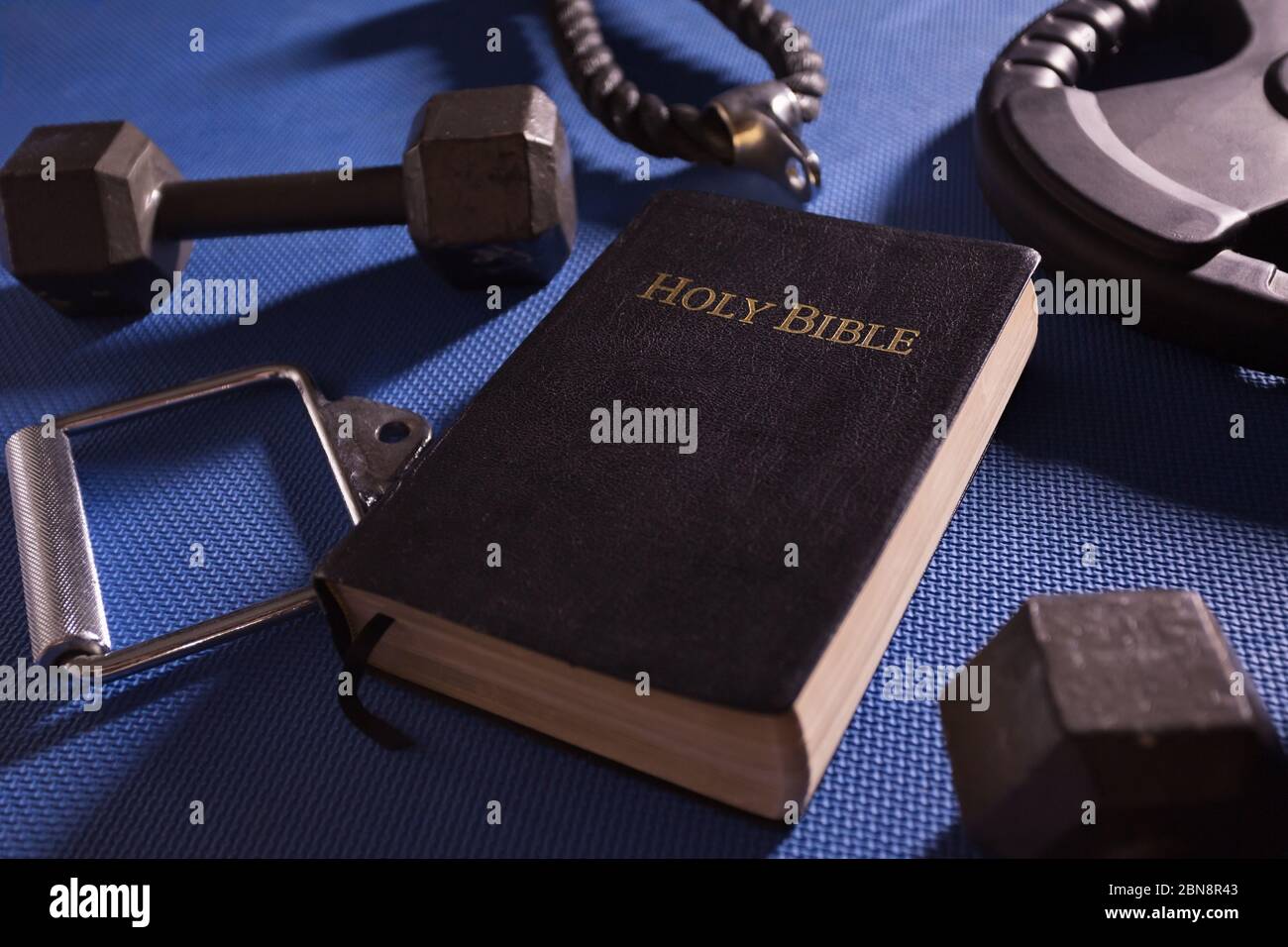 Holy Bible surrounded by dumbbells weights and other exercise equipment ...
