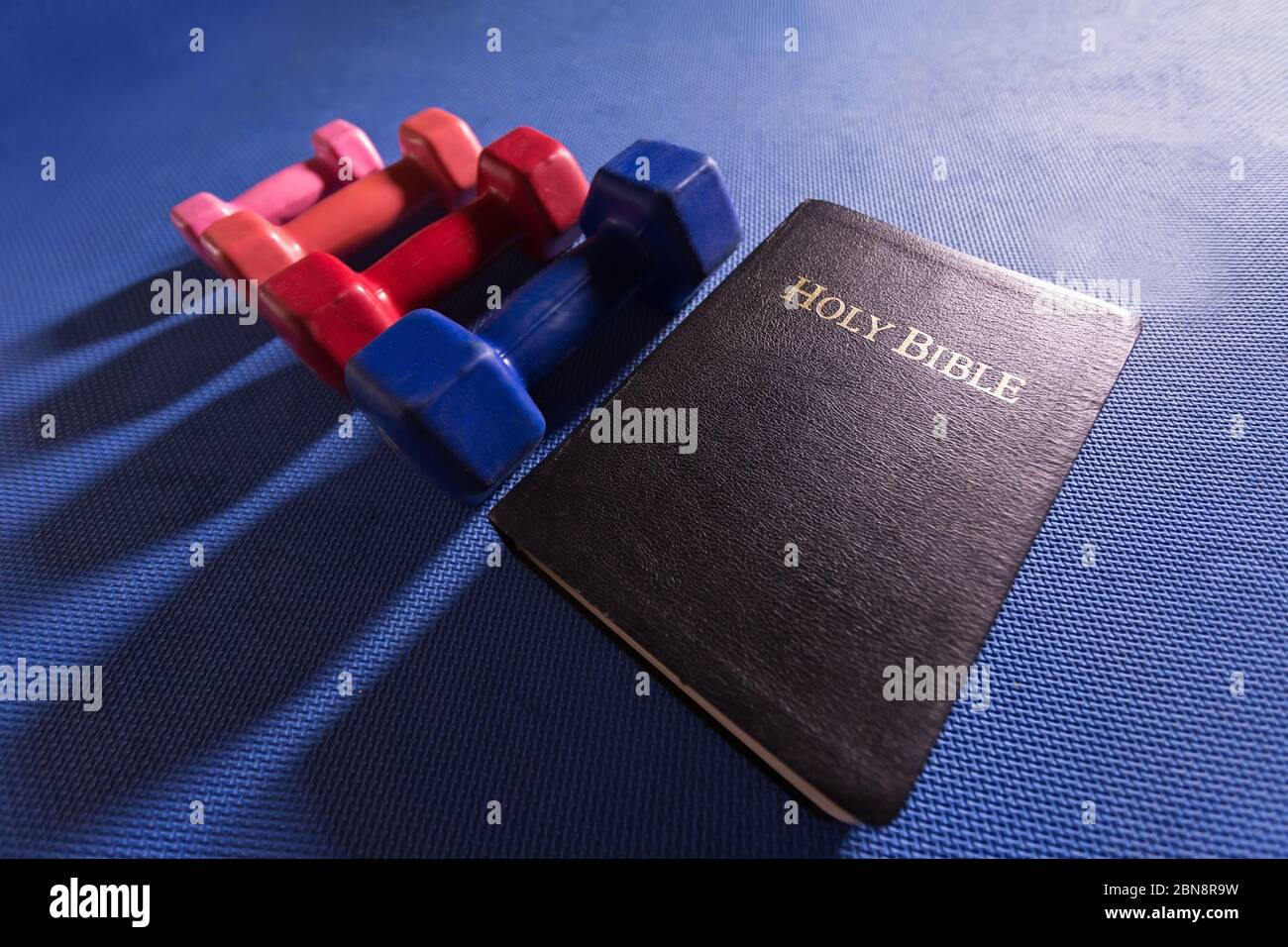 Dumbbells on a blue gym workout mat next to the Holy Scriptures Stock ...
