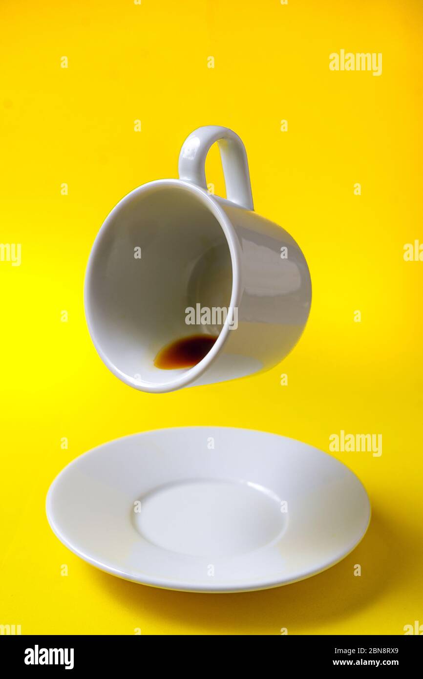 white cup of coffee with coffee floating tilted in the air and a saucer ...