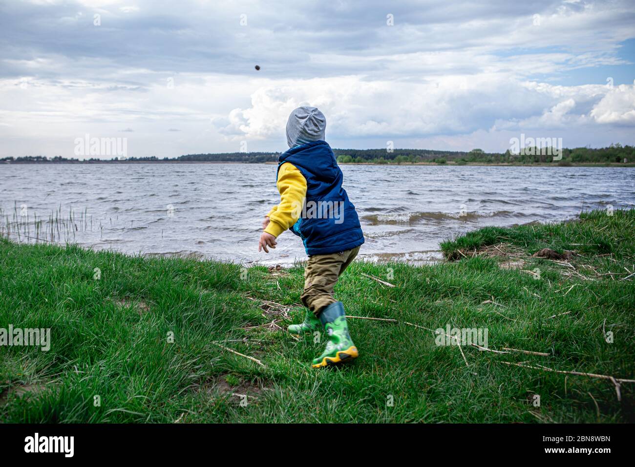 little kid throwing rocks in lake. rubber boots Stock Photo - Alamy