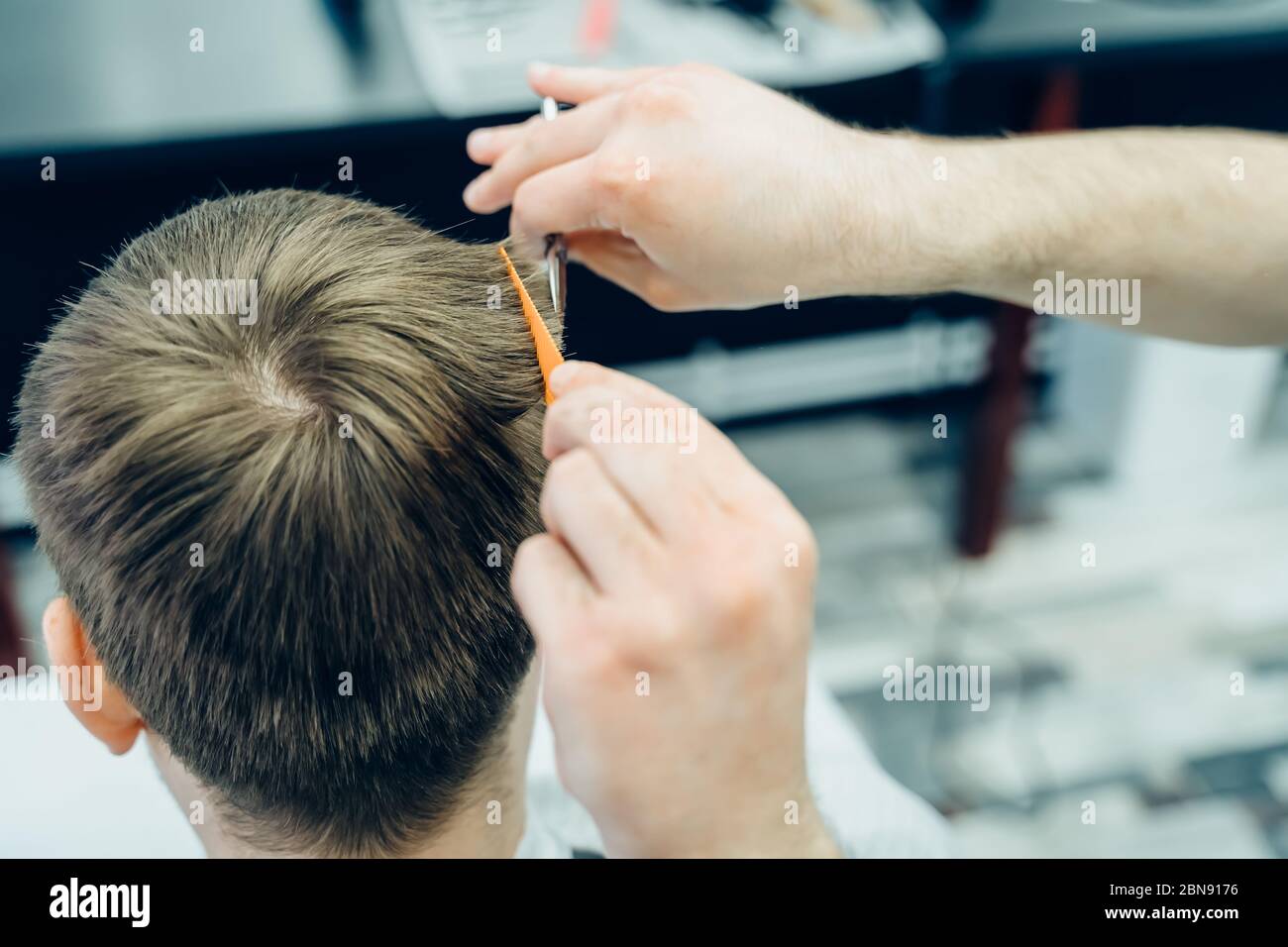 Tattooed Barber cuts the hair of the client with scissors. Close up ...