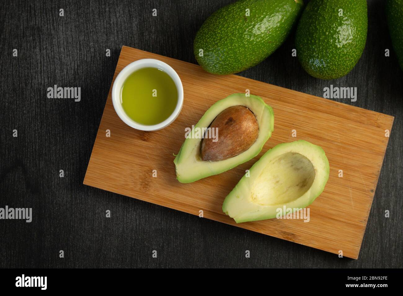 Fresh sliced avocado and olive oil on wooden background. Cosmetic oils ...