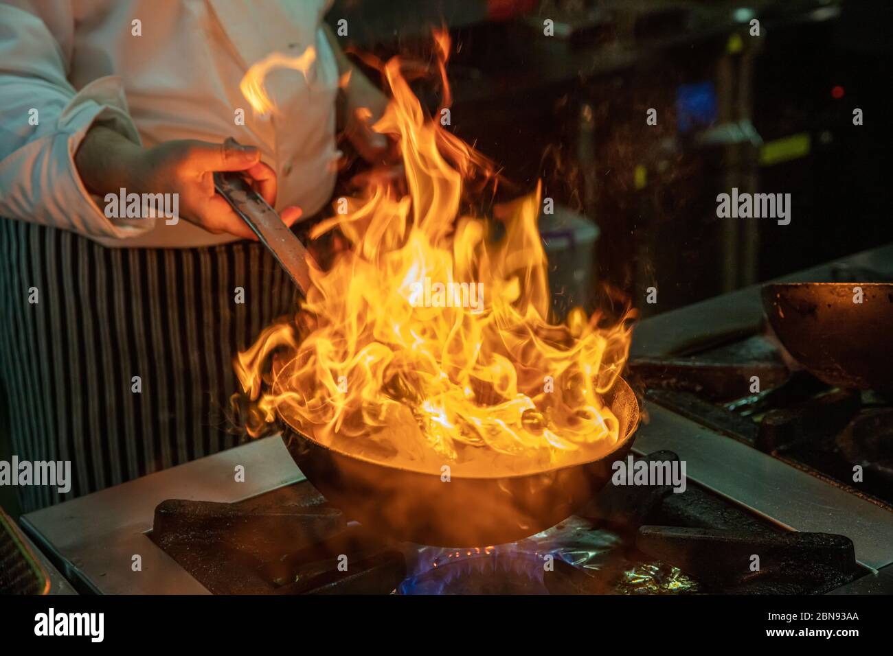 Chef Cooking With Fire In Frying Pan. Professional chef in a commercial ...