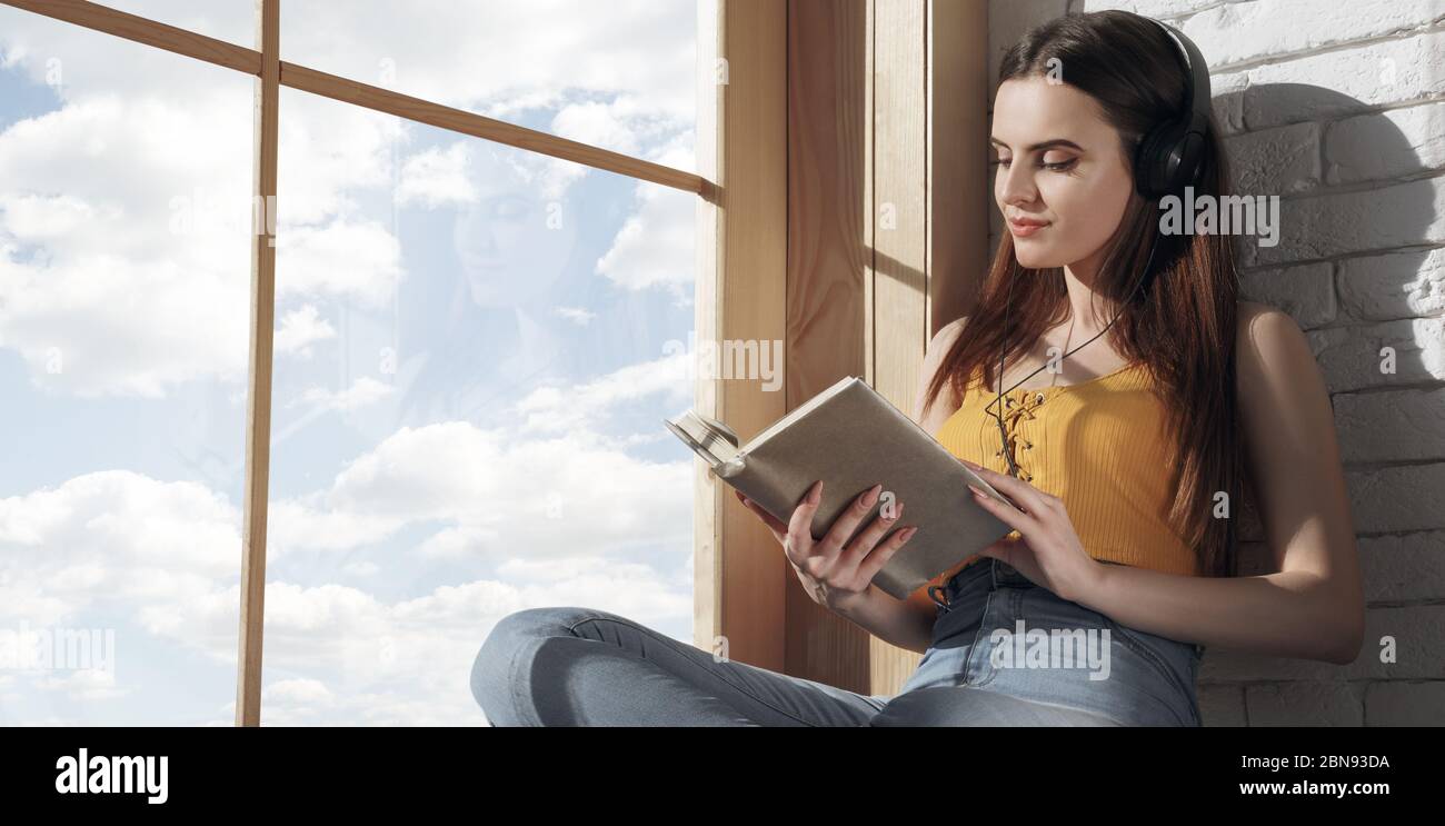 Panoramic shot of young girl reading a book while sitting on window ...