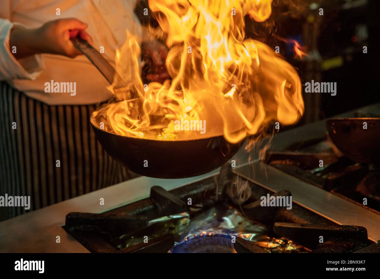 Chef Cooking With Fire In Frying Pan. Professional chef in a commercial ...