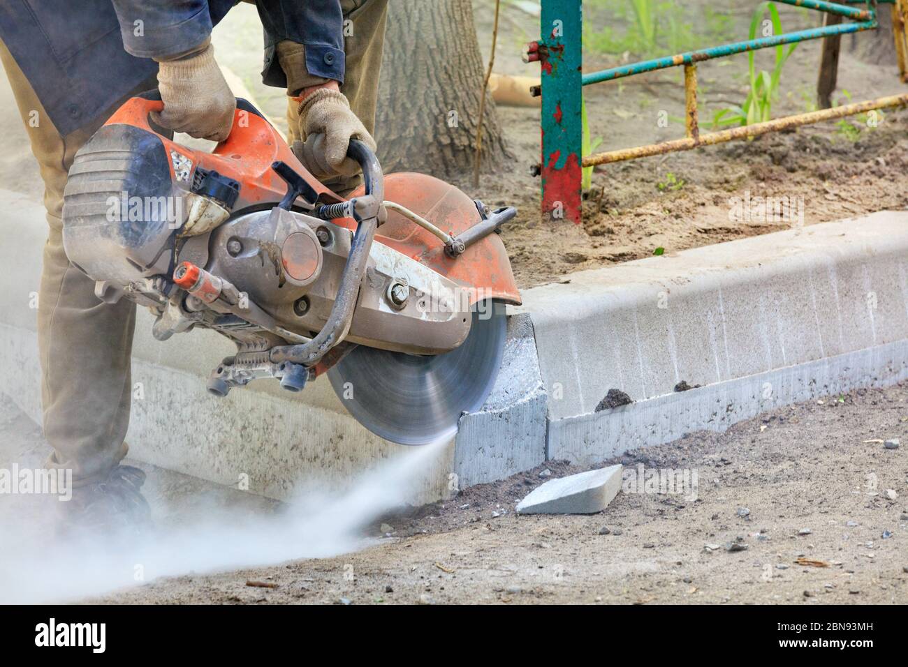 A worker using a concrete cutter cuts concrete curbs in a cloud of ...