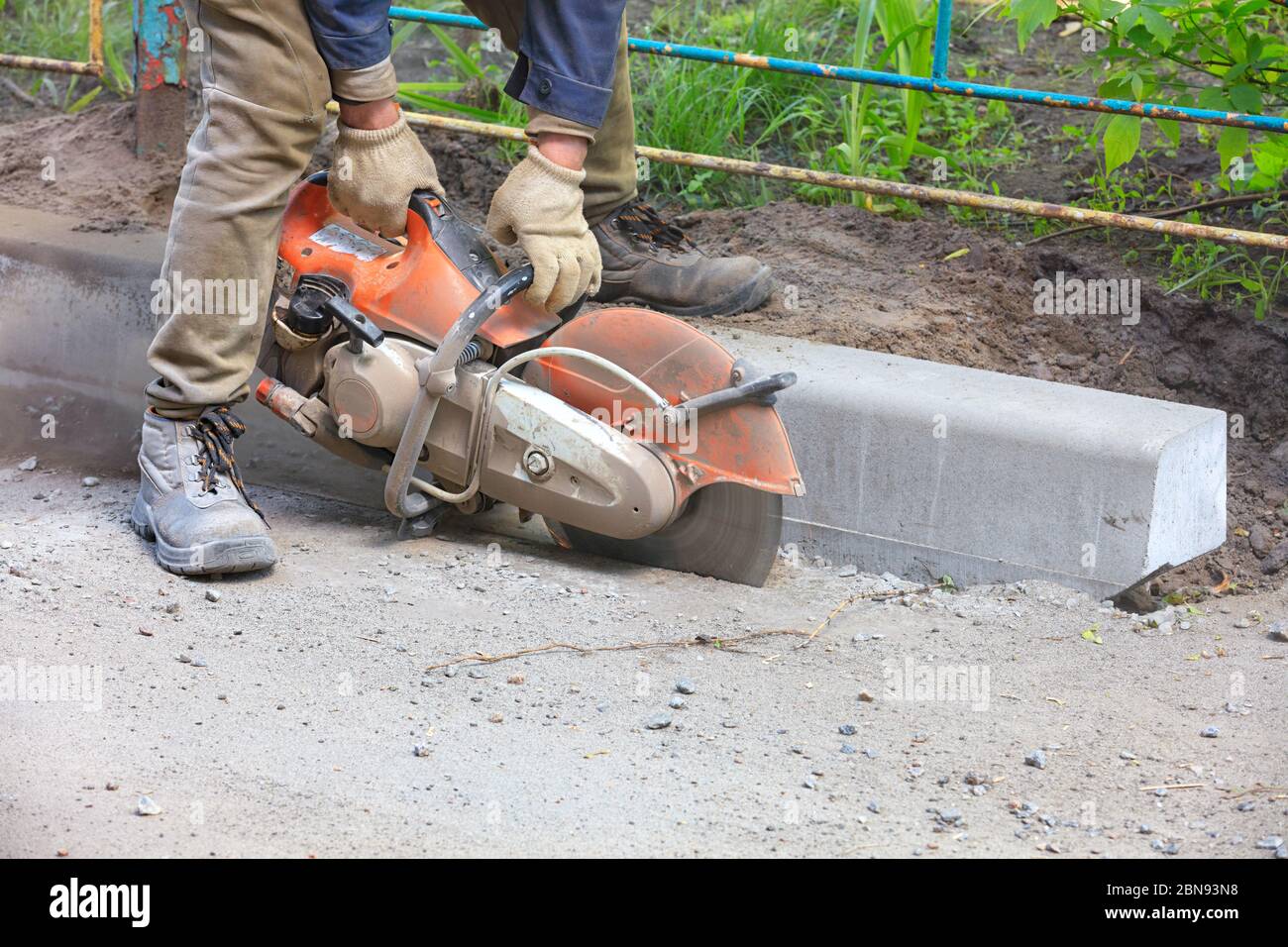 A worker using a concrete cutter cuts asphalt and concrete curbs in a ...