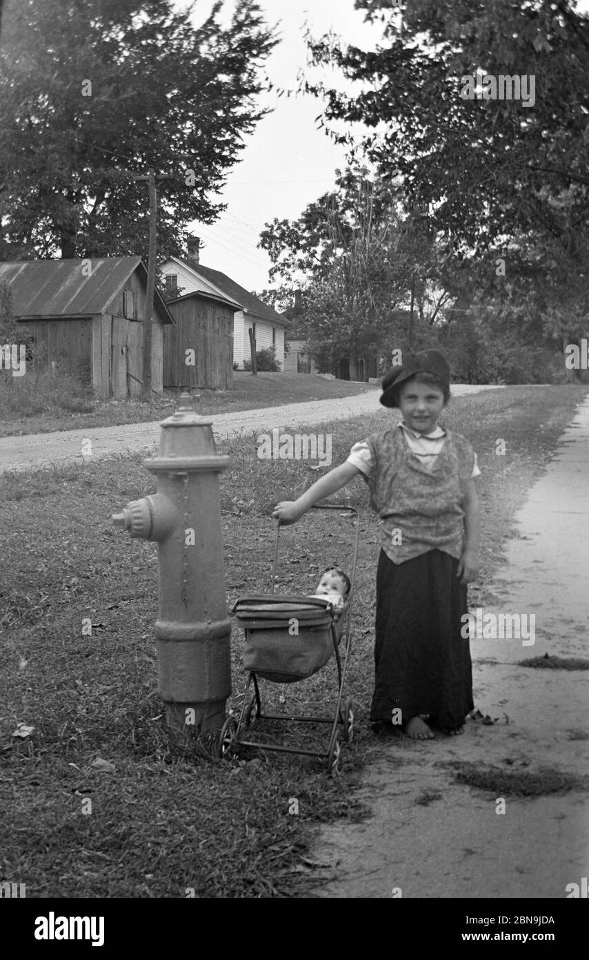 A little girl with a baby stroller on a sidewalk next to a fire hydrant ...