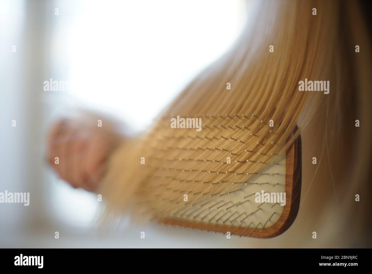 Female hand combing long blond hair with wooden shovel comb close-up ...