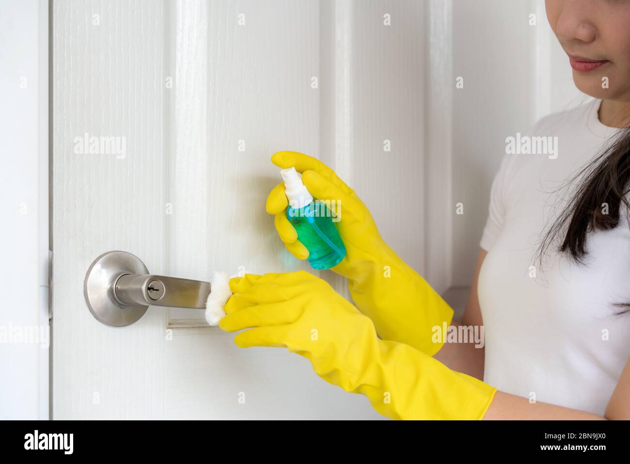 Asian woman disinfecting the door knobs by spraying a blue sanitizer ...